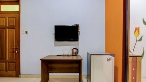 Quarto com escrivaninha de madeira, geladeira branca, televisão fixada na parede e porta com placa.