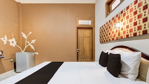 Quarto de hotel com uma cama, mesa de cabeceira, luminária na parede e uma porta.