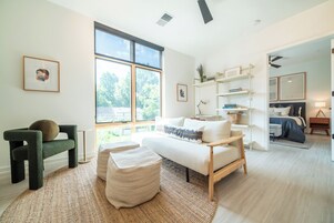 Uma sala de estar moderna com uma janela grande, um sofá verde, um sofá branco, uma mesa de centro de madeira e uma estante.