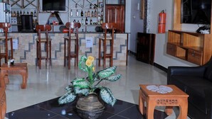 Sala de estar com sofás de couro preto, mesas de centro de madeira e uma planta central.