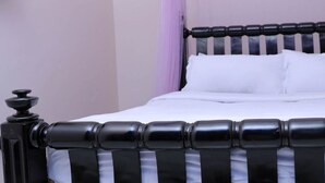 Uma cama com cabeceira listrada em preto e branco, roupa de cama branca e uma mesa de cabeceira com abajur.