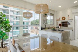 Cozinha moderna com uma ilha grande, armários brancos e vista para um edifício através de amplas janelas.