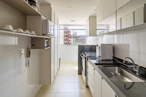 Uma cozinha moderna com armários brancos, bancada preta e janela com vista para edifícios.