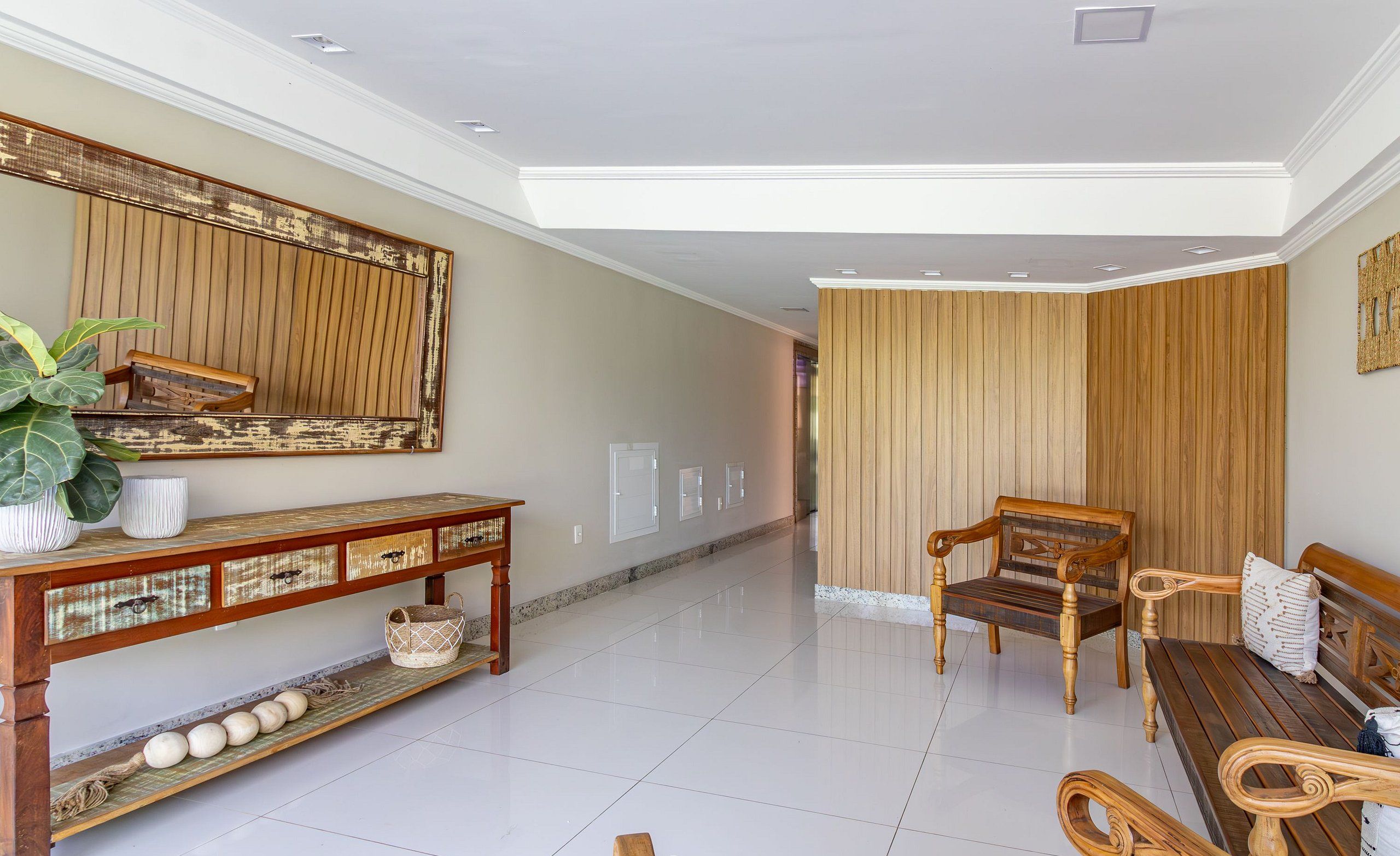 Um corredor espaçoso com um banco de madeira, uma mesa de consola com objetos decorativos e um espelho grande na parede.
