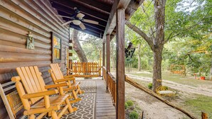 Uma cabana de madeira com varanda, cadeiras de balanço e área coberta com ventilador de teto.