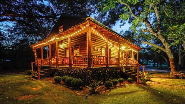 Uma cabana de madeira com varanda, rodeada por árvores e iluminada por luzes de Natal.