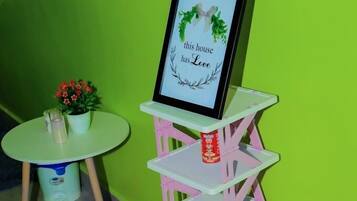 Quarto com parede verde, uma pequena mesa redonda com planta em vaso e um aparador branco com placa emoldurada.