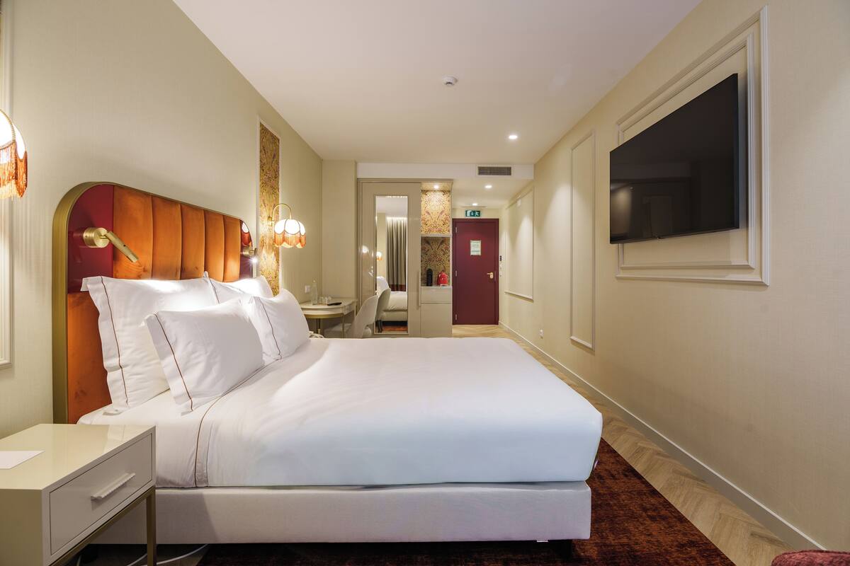 Quarto de hotel com uma cama grande, mesas de cabeceira, escrivaninha, televisão e um banheiro visível por uma porta aberta.