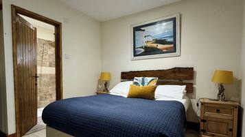 Quarto com cama, cabeceira de madeira, duas mesas de cabeceira com luminárias, um quadro na parede e uma porta que dá para outro cômodo.