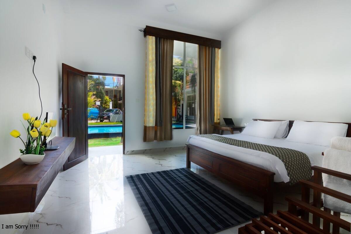 Quarto com cama, mesa de cabeceira, abajur e vista para uma piscina.