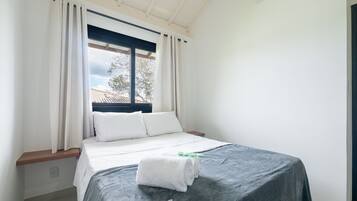 Quarto com cama, cortinas brancas, uma janela e uma toalha sobre a cama.
