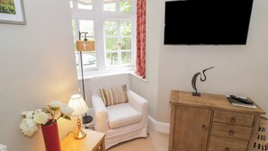 Um quarto aconchegante com uma cama, uma TV fixada na parede, um armário de madeira e uma janela com cortinas.