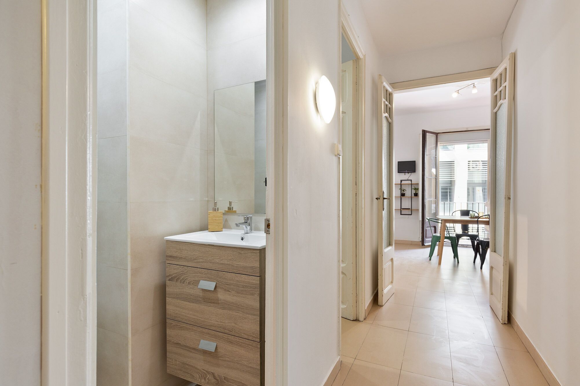 Um corredor com toucador de madeira, um espelho e uma porta que dá para uma varanda com mesa e cadeiras.
