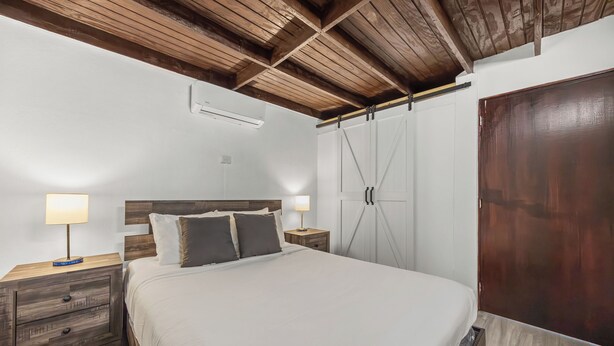 Quarto com teto de madeira, cama com roupa de cama branca, duas mesas de cabeceira com luminárias e um guarda-roupa com espelho.