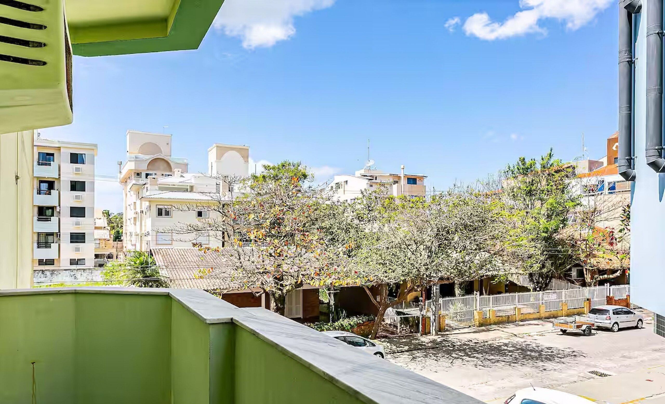 Uma área residencial com edifícios altos, uma rua com carros estacionados e árvores com poucas folhas.