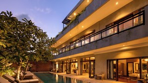 Um edifício moderno com vários andares, piscina, área de estar ao ar livre e varanda com plantas.