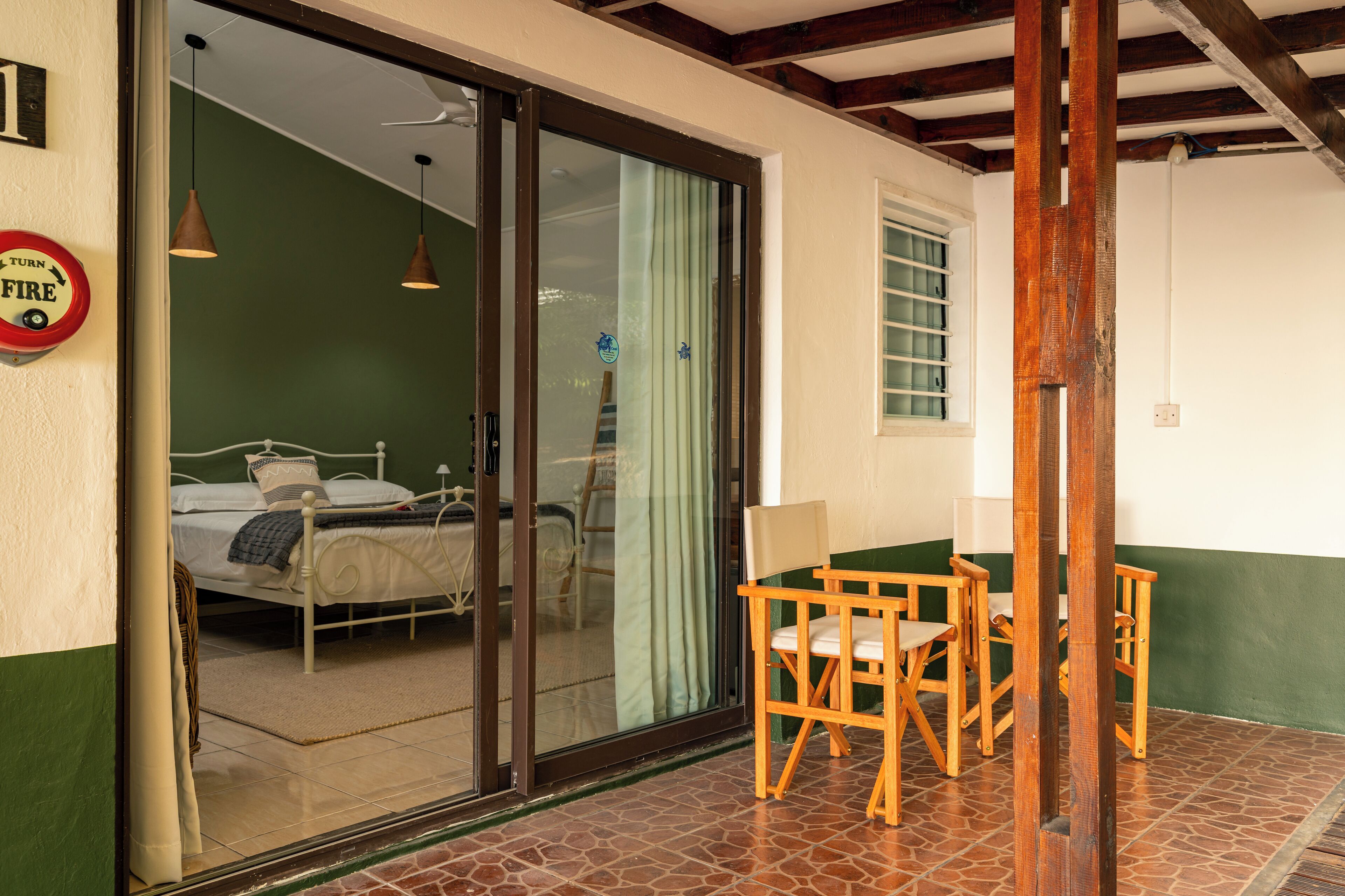Quarto com cama, cadeira, mesa e porta de vidro deslizante que dá para uma varanda.