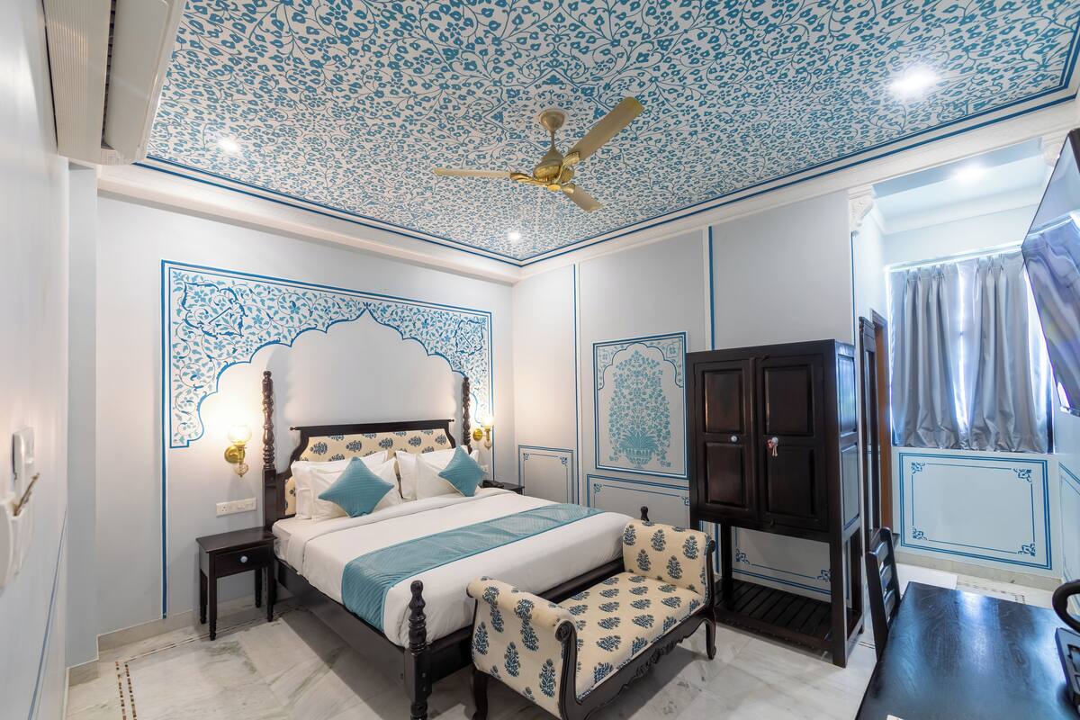 Quarto com cama, mesas de cabeceira, uma cadeira, guarda-roupa e ventoinha no teto.