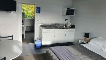 Quarto de hotel compacto com cozinha compacta, cama, mesa pequena e uma cadeira.