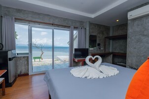 Quarto de hotel com cama, televisão, escrivaninha e vista para a praia.