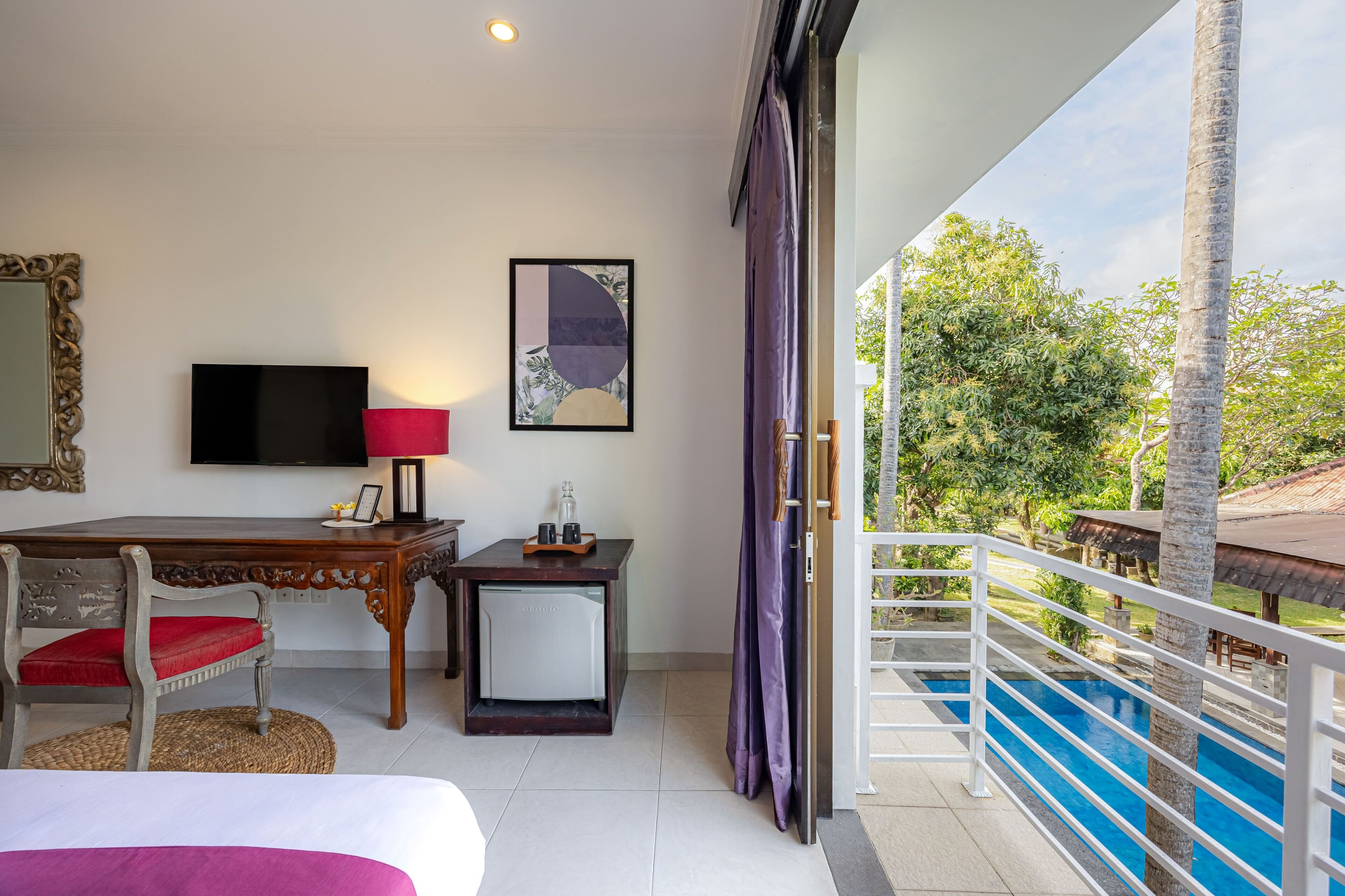 Quarto de hotel com cama, escrivaninha, televisão, mini-geladeira e varanda com piscina.