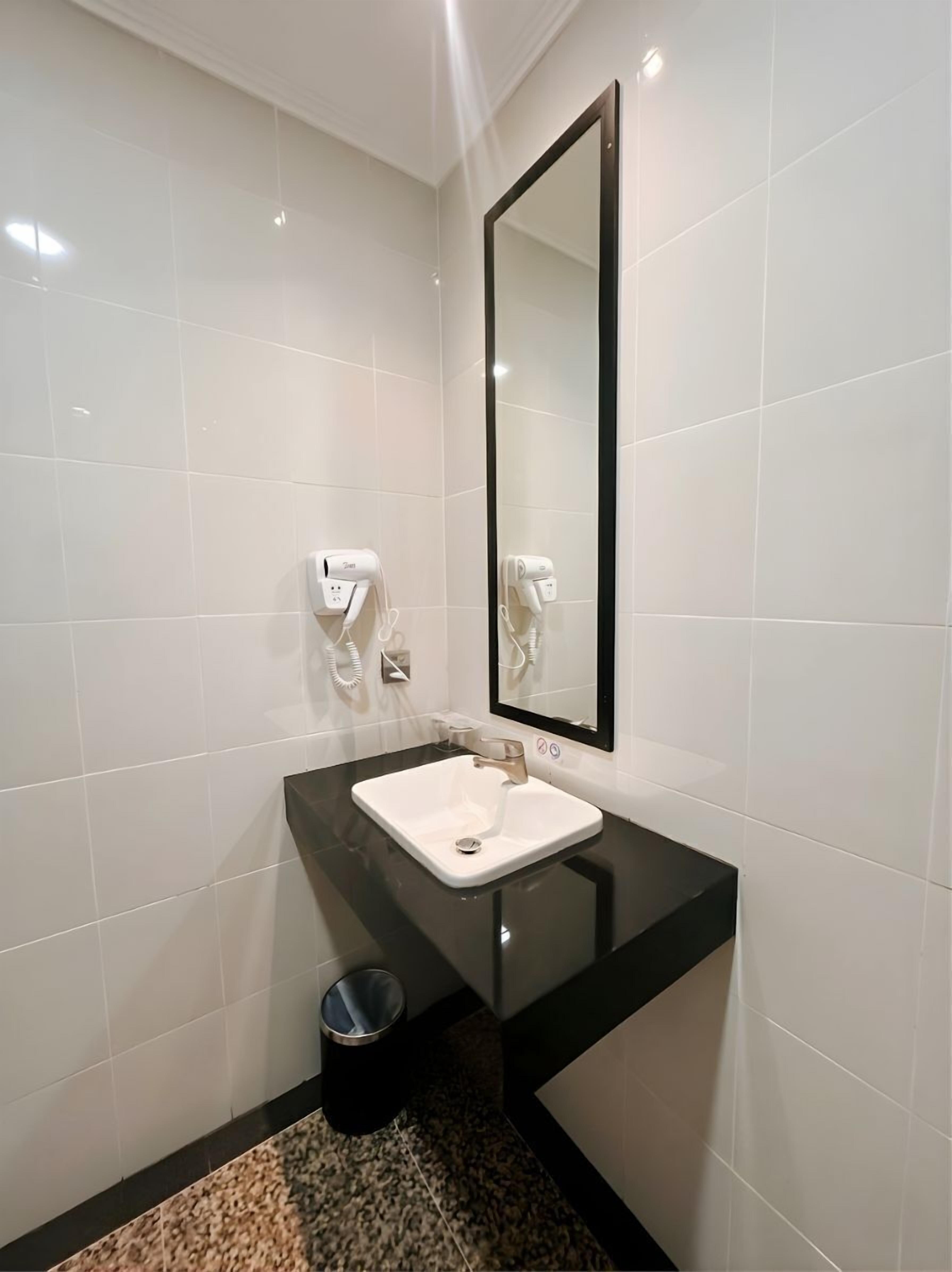 Casa de banho moderna com bancada preta, lavatório branco e um espelho grande.