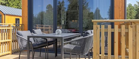 Um deck de madeira com uma área de varanda envidraçada, mobiliado com uma mesa e cadeiras.