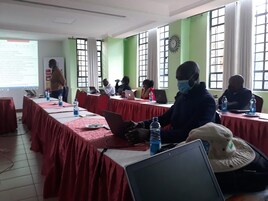 Sala de conferências com mesas, laptops e garrafas de água.