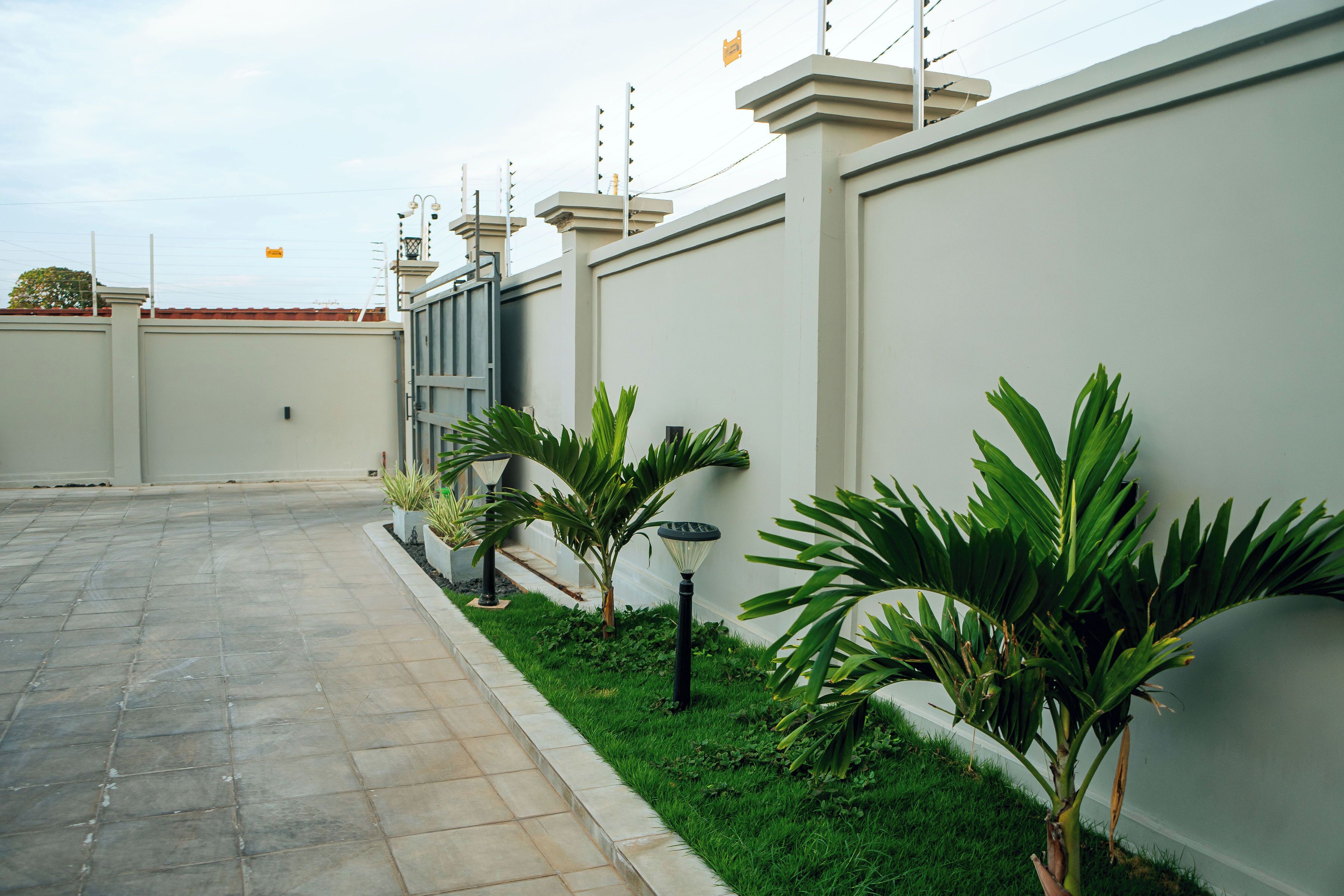 Uma passarela pavimentada com um pequeno muro de um lado e uma área gramada com plantas do outro.