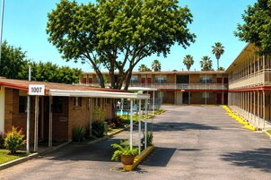 Um motel com área de estacionamento coberta, uma grande árvore e piscina.