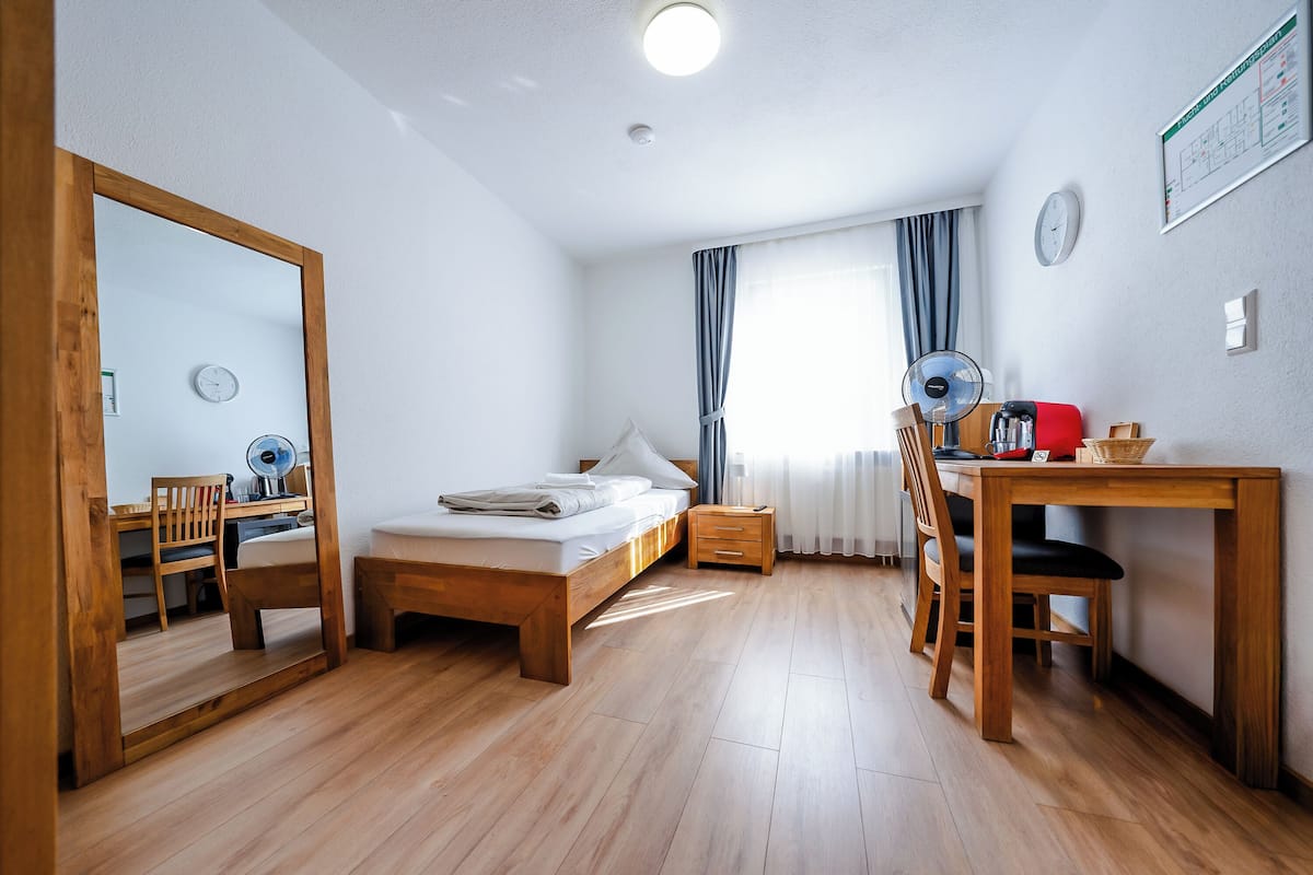 Quarto com cama de madeira, mesa de cabeceira e escrivaninha com cadeira.