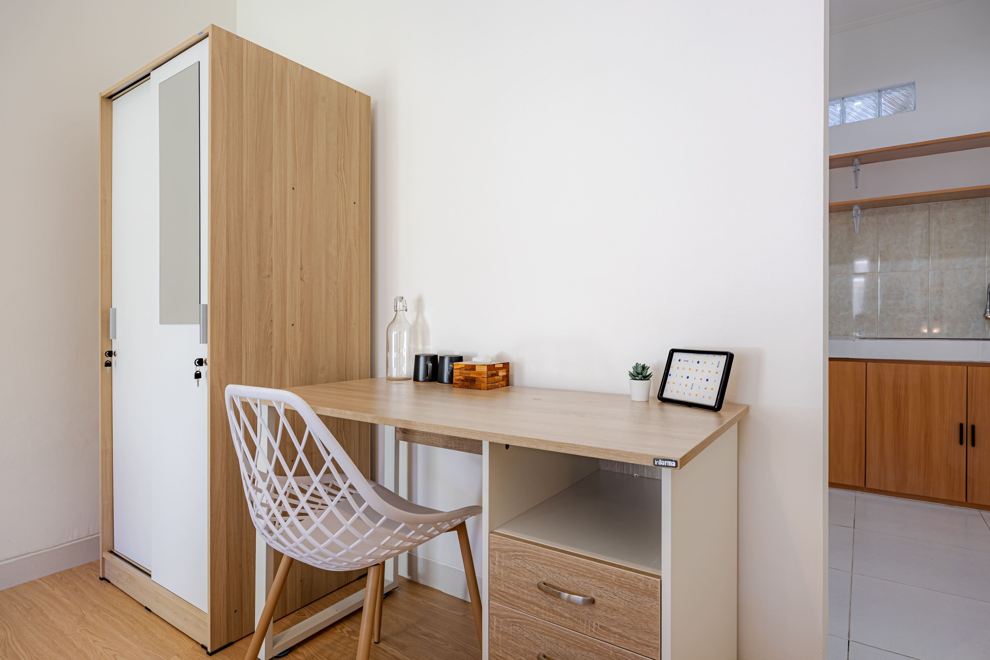 Quarto compacto com uma escrivaninha de madeira, uma cadeira branca, uma pequena planta e um quadro emoldurado.