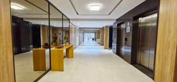 Corredor de hotel com piso de madeira, paredes espelhadas e uma fileira de elevadores.