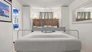 Uma cama com cabeceira, uma mesinha de cabeceira, um espelho e um quadro na parede.