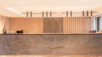 Uma área de recepção com painel de parede de madeira, balcão de mármore e luminária moderna.