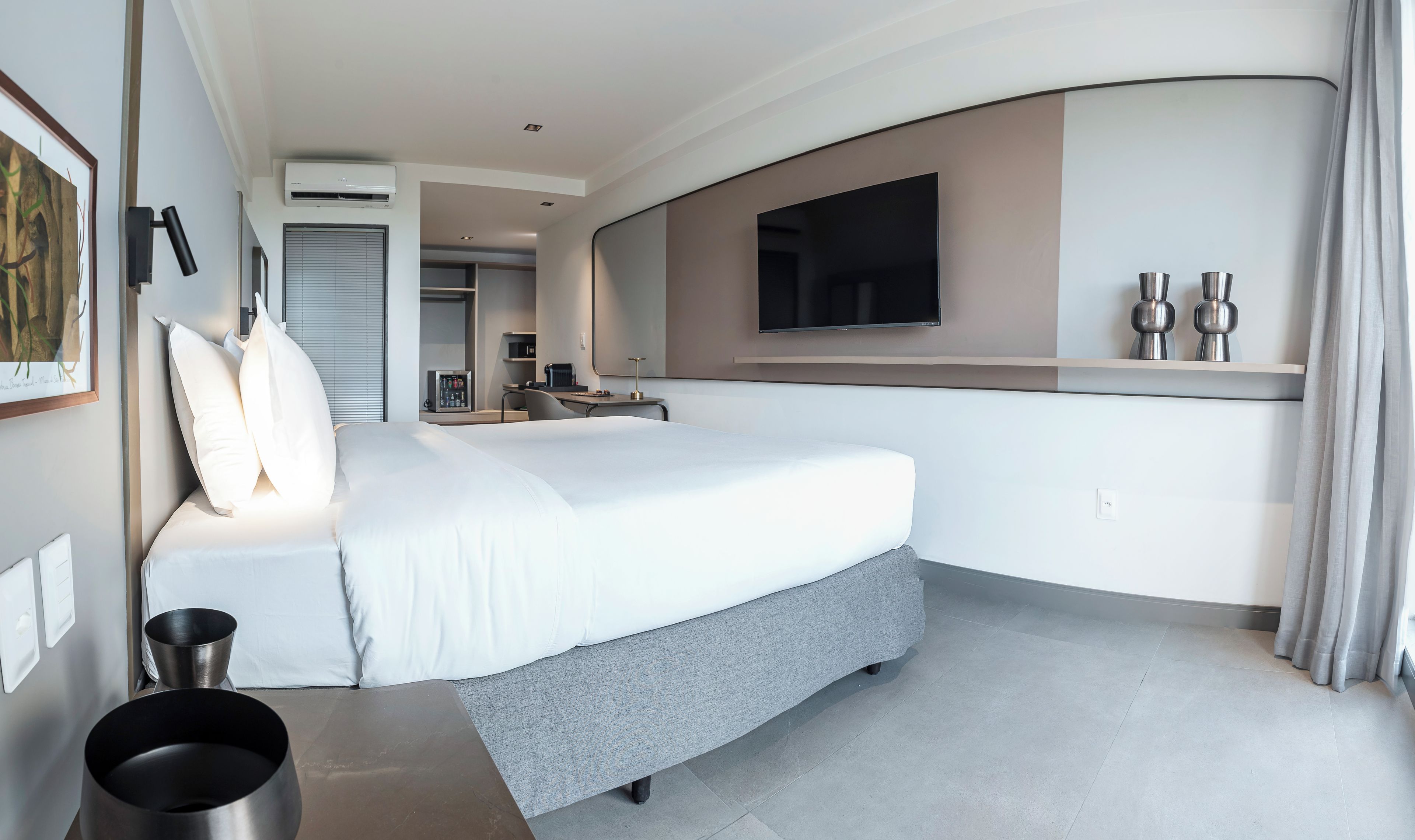 Quarto de hotel moderno com cama grande, televisão de tela plana, escrivaninha e closet espaçoso.