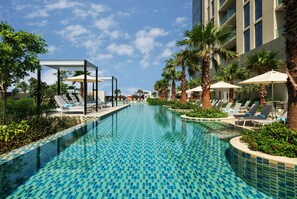 Piscina com padrões em azulejos, cercada por palmeiras e espreguiçadeiras.