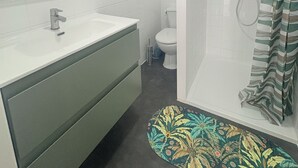 Uma casa de banho moderna com lavatório branco, espelho e chuveiro.