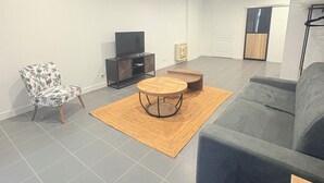 Uma sala de estar moderna com um sofá cinzento, uma poltrona estampada, uma mesa de centro e uma televisão de tela plana.