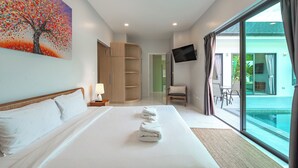 Quarto de hotel com uma cama grande, um quadro de uma árvore, uma televisão e vista para uma piscina.