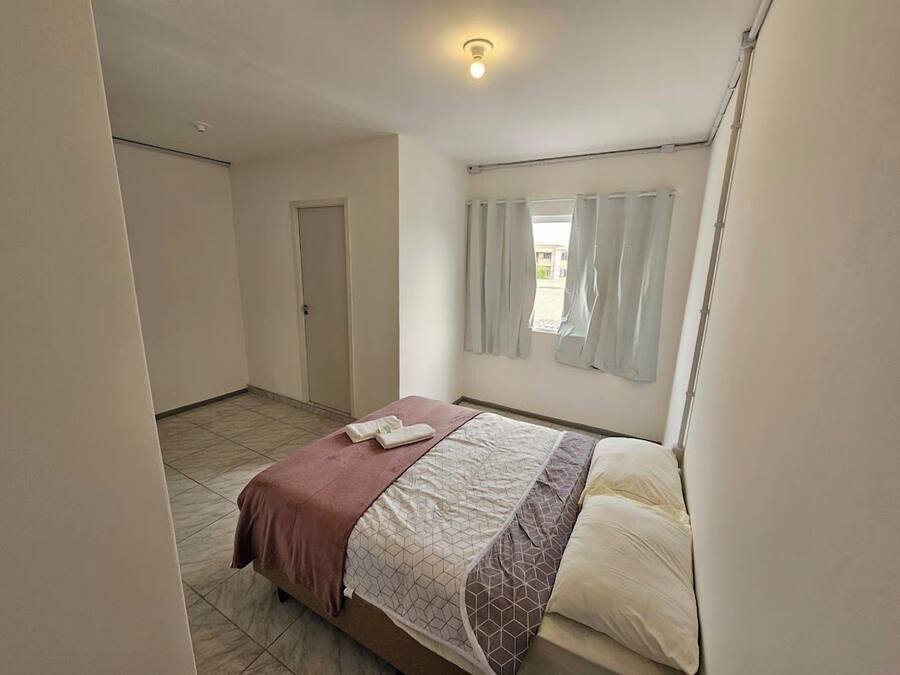 Quarto com cama, porta e janela com cortinas.