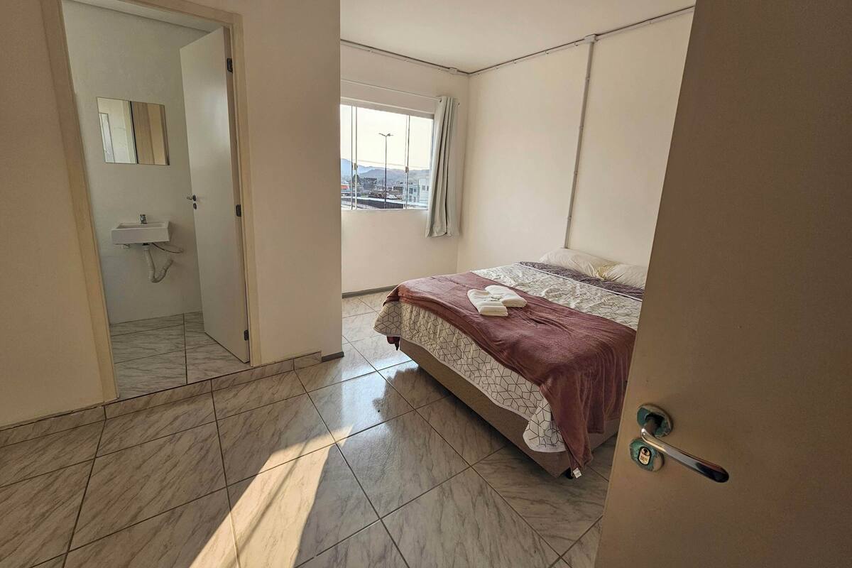 Quarto de hotel com cama, banheiro com pia e vista da cidade pela janela.