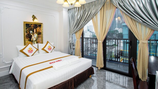 Quarto de hotel com uma cama grande, varanda com cortinas, um quadro na parede e um lustre.