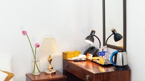 Uma mesa de madeira com uma lâmpada, um telefone, uma chaleira e um vaso com flores.