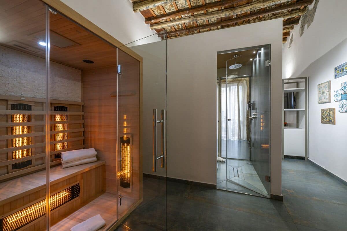Um spa moderno com divisória de vidro, bancos de madeira e área de chuveiro aparente.