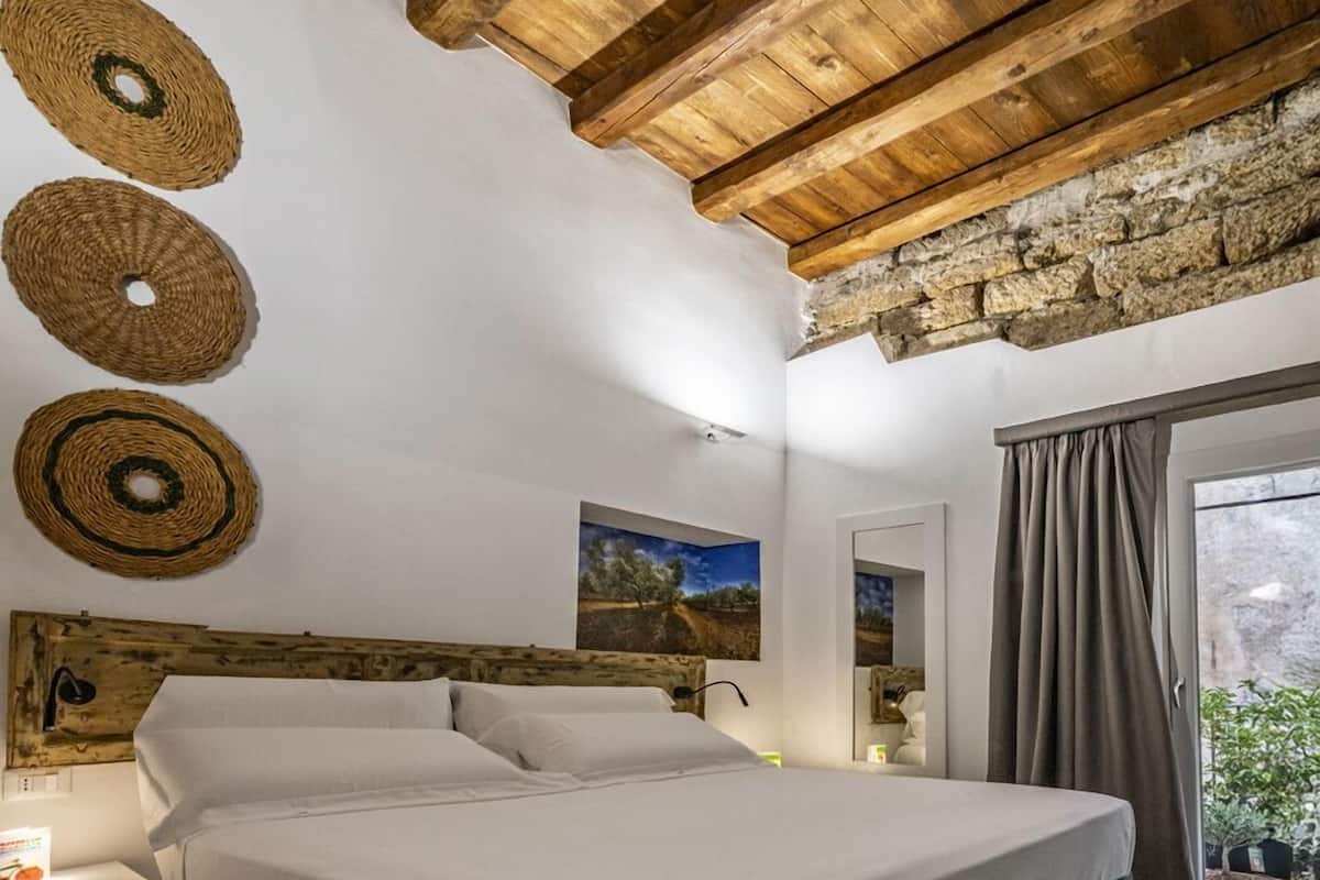 Quarto com teto de madeira, uma cama, mesa de cabeceira, espelho e janela com cortinas.