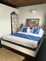 Quarto com uma cama grande, uma mesinha de cabeceira, um quadro e teto de madeira.
