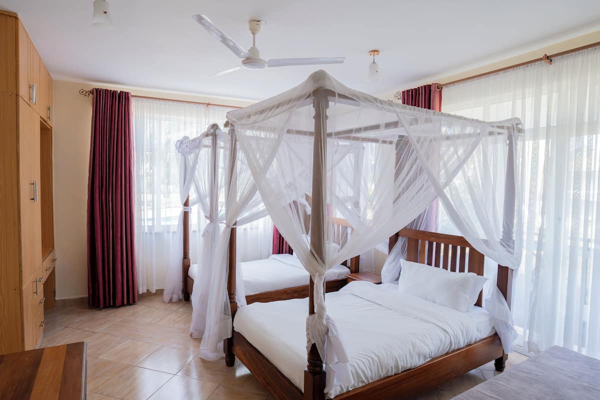 Uma cama de dossel com cortina, roupa de cama branca, um guarda-roupa de madeira e um ventilador de teto em um quarto de hotel.