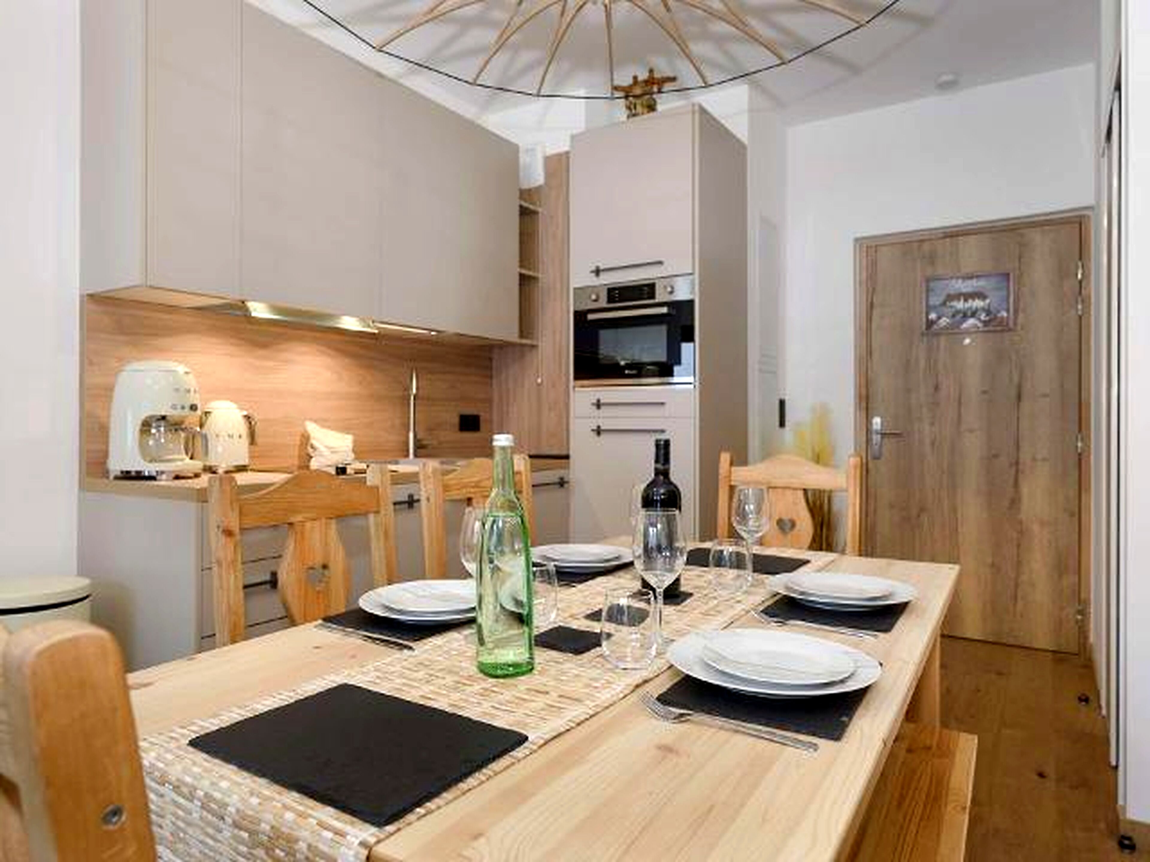 Cozinha compacta com eletrodomésticos modernos, uma mesa de jantar para quatro pessoas e uma porta de madeira com uma ilustração.