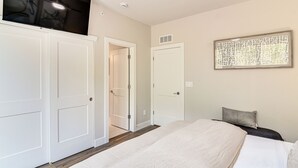 Quarto com uma cama, ventoinha no teto, televisão de tela plana e uma obra de arte emoldurada na parede.